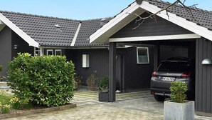 Um edifício residencial com garagem, um carro estacionado dentro e um jardim bem cuidado com diversas plantas.