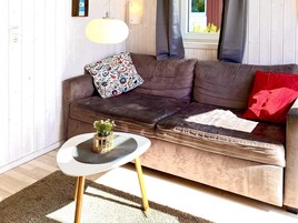 Uma sala de estar com um sofá marrom, uma mesa branca com um vaso e uma janela com cortinas.