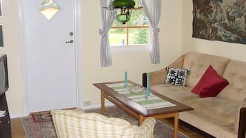 Uma sala de estar com um sofá bege, uma mesa de centro de madeira, uma poltrona de vime e um quadro na parede.