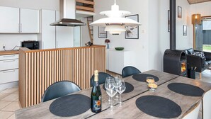 Cozinha moderna com ilha de madeira, área de jantar com mesa posta para quatro e fogão a lenha embutido.