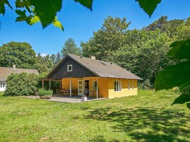 Uma casa térrea com varanda, cercada por gramado e árvores.