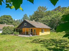 Uma casa térrea com varanda, cercada por um gramado e árvores.