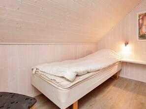 Uma cama de solteiro com cabeceira, mesa de cabeceira com luminária e piso de madeira.
