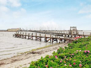 Um cais se estendendo sobre águas calmas, com um edifício e barcos atracados ao fundo.