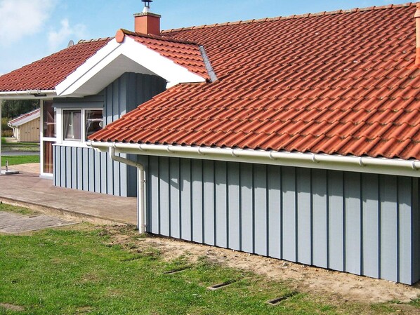 Um edifício residencial com telhado de telhas vermelhas, fachada cinzenta e chaminé visível.