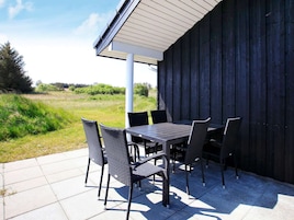 Um pátio externo com mesa e cadeiras, um pilar branco e vista para um campo gramado.
