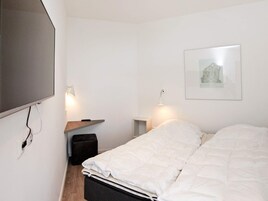 Quarto com cama, mesas de cabeceira, televisão na parede e um quadro emoldurado.