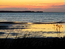 Um pôr do sol sobre águas calmas, com uma linha de costa distante.