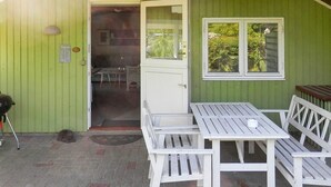 Área externa coberta com mesa e bancos, porta que dá para um espaço interno e janela com vista para o verde.