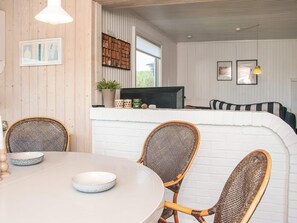 Uma sala de jantar com uma mesa redonda e cadeiras de vime, uma parede de tijolos brancos e uma televisão preta em uma prateleira.