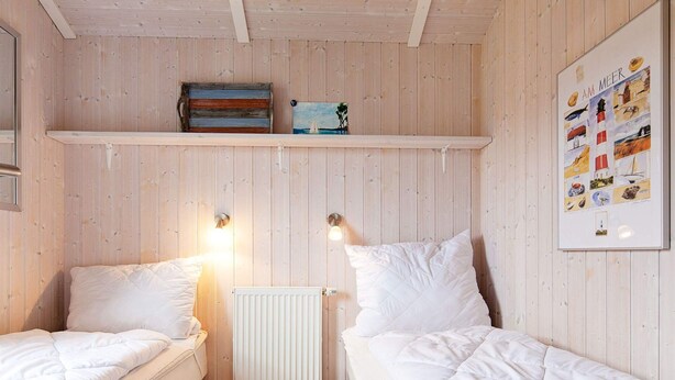 Quarto com duas camas, teto de madeira, radiador branco e um quadro pendurado na parede.