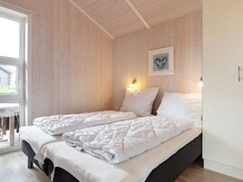 Quarto com duas camas, paredes de madeira, um quadro e uma janela.