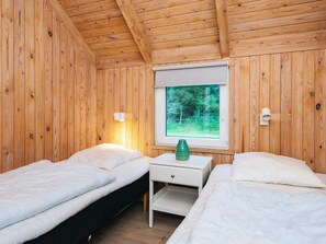 Quarto de cabana com duas camas, janela com vista para árvores e mesa de cabeceira com abajur.