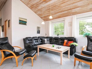 Uma sala de estar moderna com um sofá de couro preto, cadeiras de madeira, uma mesa de centro de madeira e teto com vigas de madeira aparente.