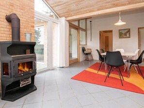 Interior moderno com lareira a lenha, área de refeições com cadeiras e mesa, e uma grande janela que proporciona luz natural.