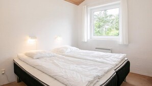 Quarto com cama, duas luzes de parede, janela com cortinas e radiador.