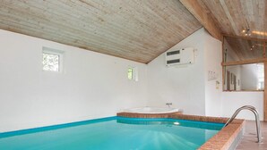 Piscina com água azul cristalina, cercada por uma borda de tijolos e um teto de madeira.