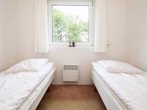 Acomodação pequena, com um quarto e duas camas de solteiro, janela com vista para árvores e aquecedor fixado na parede.