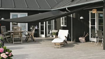 Um terraço ao ar livre com móveis de madeira, incluindo cadeiras e uma mesa, e uma área coberta com telhado.