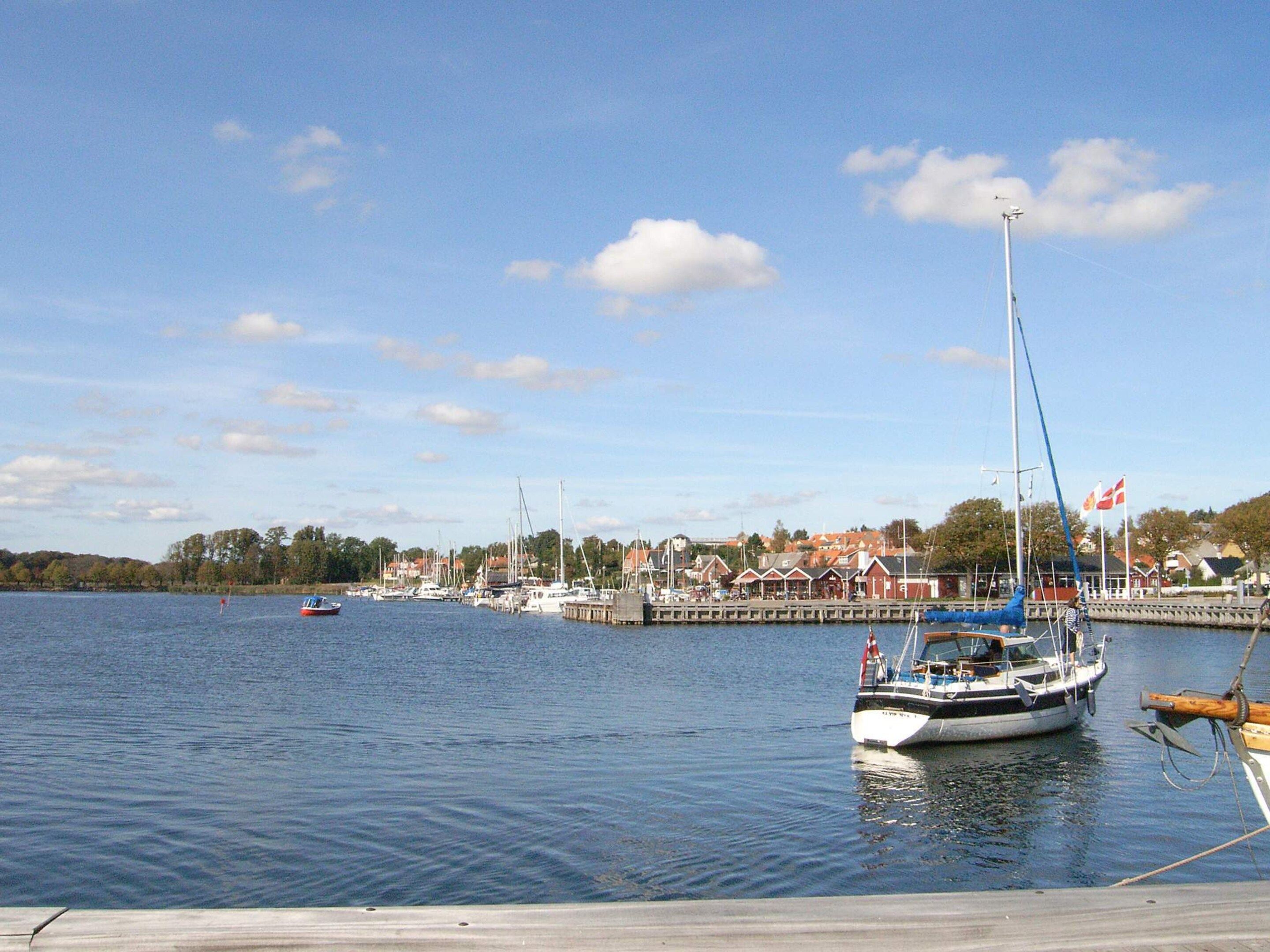 Marina com barcos atracados, céu claro e edifícios ao fundo.