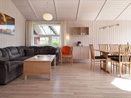 Uma sala de estar moderna com um sofá seccional, uma mesa de centro, uma mesa de jantar com cadeiras, um armário com uma cafeteira e um quadro na parede.