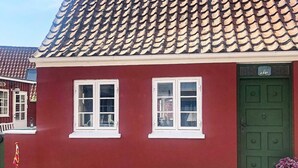 Um prédio vermelho com duas janelas emolduradas por branco e uma porta verde.