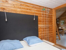 Interior de uma cabana de madeira com cama, mesa de jantar e luminária pendente.