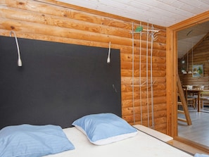 Interior de uma cabana de madeira com cama, mesa de jantar e luminária pendente.