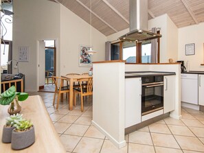 Cozinha compacta com ilha central, sala de jantar com mesa e cadeiras de madeira, e vista para o exterior através de uma janela.