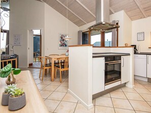 Cozinha compacta com ilha central, sala de jantar com mesa e cadeiras de madeira, e vista para o exterior através de uma janela.