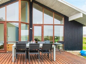 Uma área moderna para refeições ao ar livre com mesa, cadeiras, janelas amplas e um deck de madeira.
