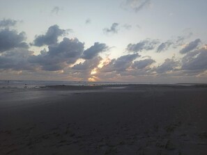 Uma praia com céu nublado e o sol se pondo ou nascendo.