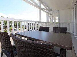 Um pátio externo com mesa e cadeiras, corrimão branco e vista para a rua.