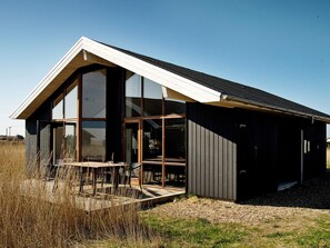 Uma casa moderna com uma ampla janela de vidro, um deck de madeira e uma entrada com calçamento de brita.