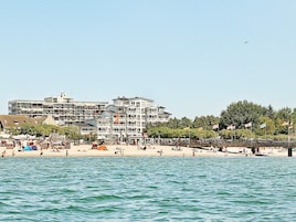 Um hotel à beira-mar com vários andares, uma praia ao primeiro plano e céu limpo.