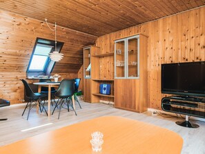 Interior em madeira com área de refeições, televisão e um armário com portas de vidro.
