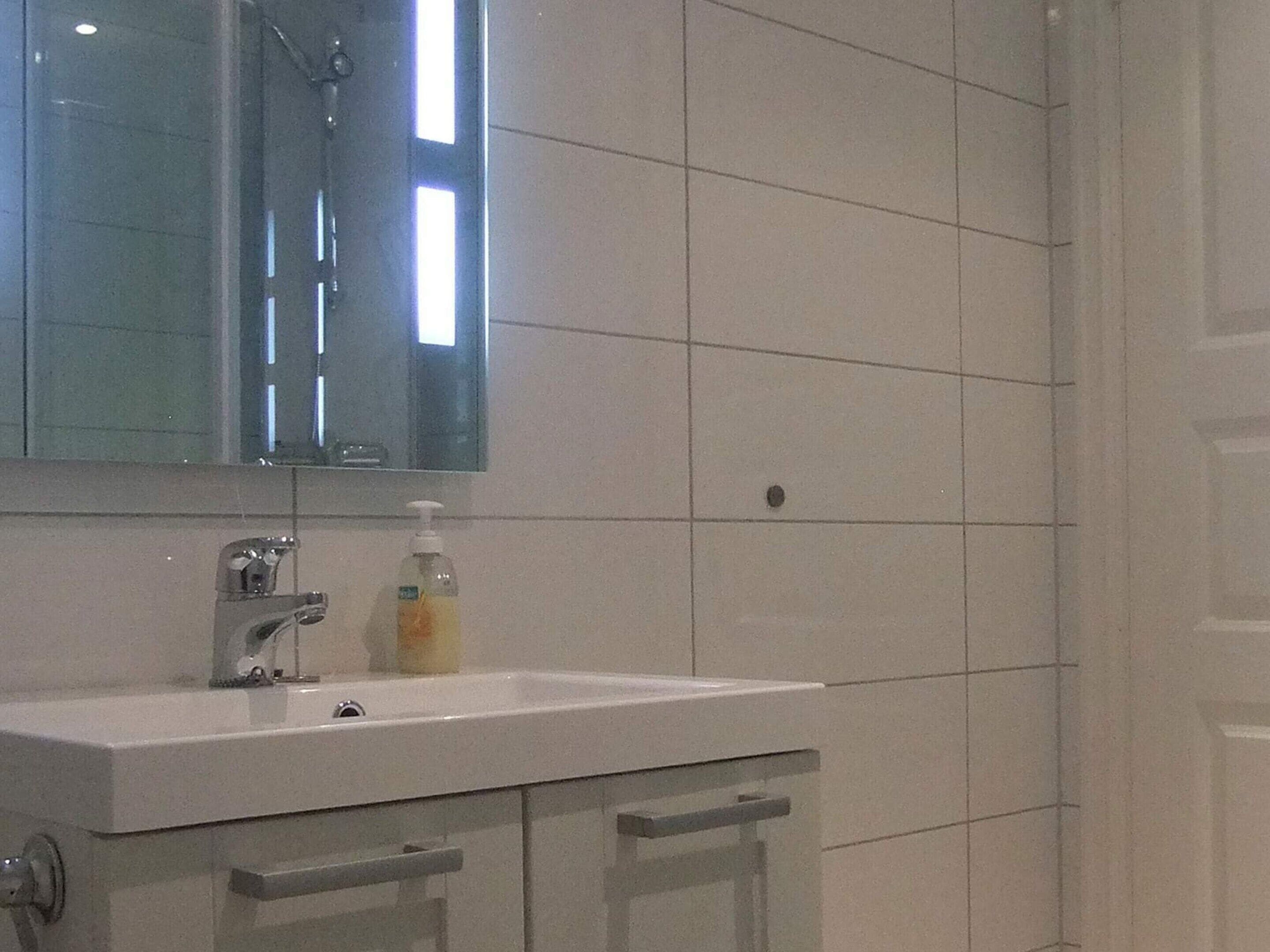 Casa de banho com lavatório branco, espelho e dispensador de sabonete.