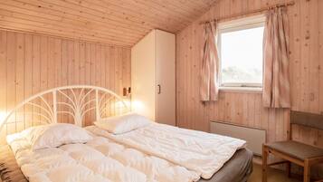 Quarto com cama, cadeira, janela com cortinas e paredes de madeira.