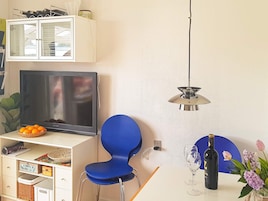 Quarto com televisão, uma cadeira azul, uma garrafa de vinho e um vaso com flores.