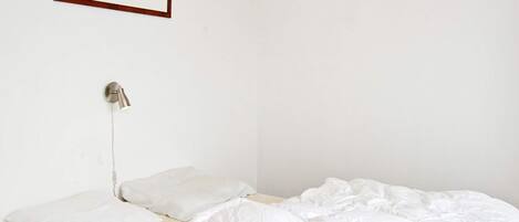 Uma cama de solteiro com roupa de cama branca e uma luminária na parede.