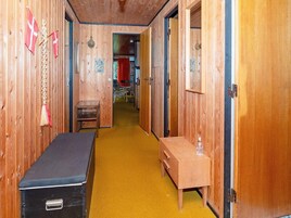 Um corredor estreito com paredes de madeira, um banco e uma pequena mesa com uma garrafa.