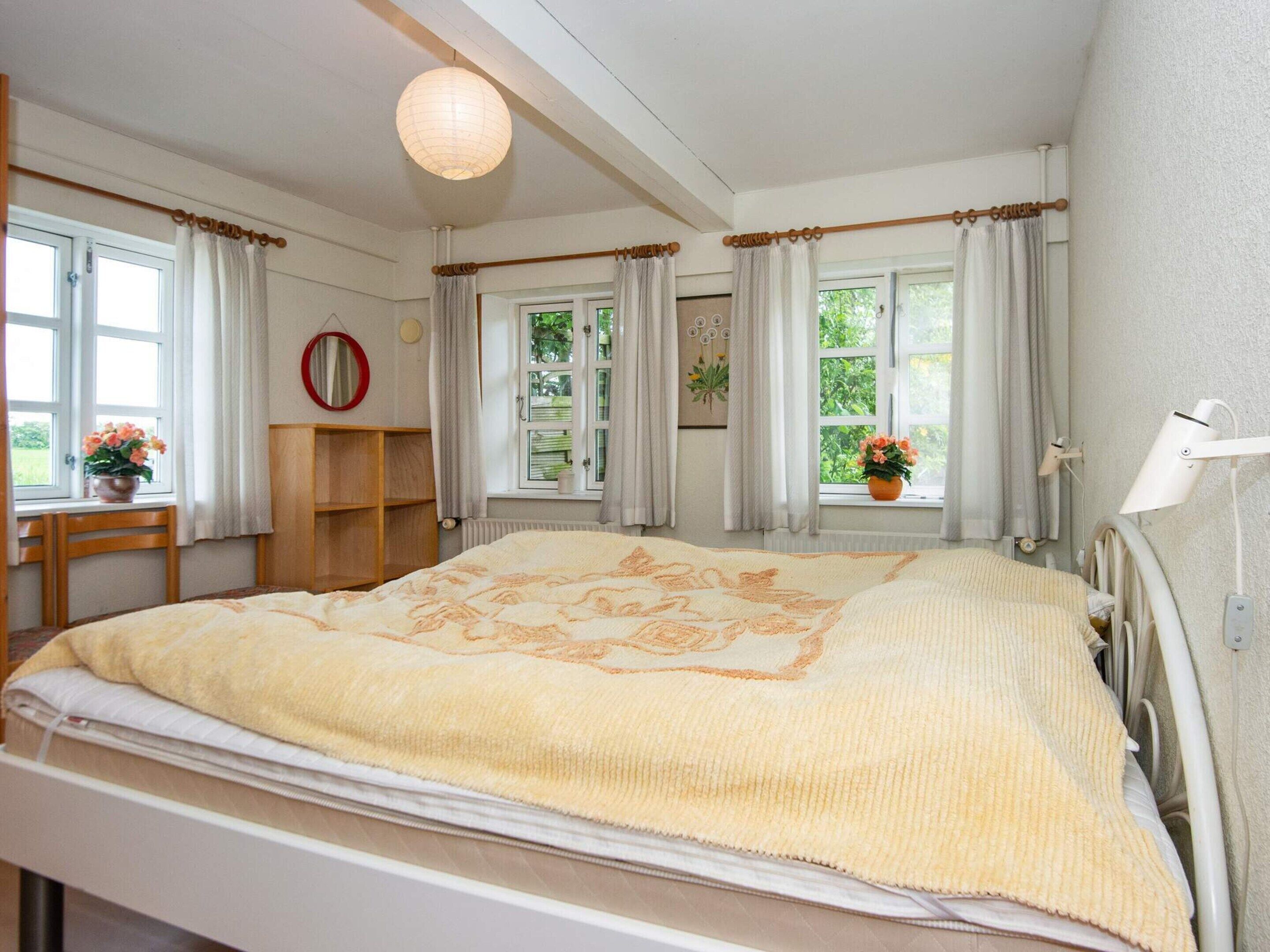 Quarto com cama grande, mesa de cabeceira, espelho e janela com cortinas.