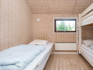 Um quarto pequeno com painéis de madeira, beliches e uma cama simples.