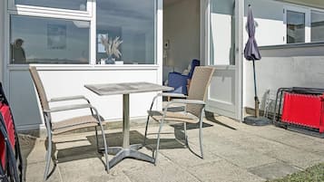 Um pátio externo com mesa, duas cadeiras, um armário vermelho e uma cadeira azul.