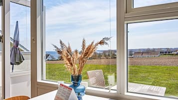 Quarto com uma grande janela, uma mesa com cardápio e vista para um campo gramado e edifícios.