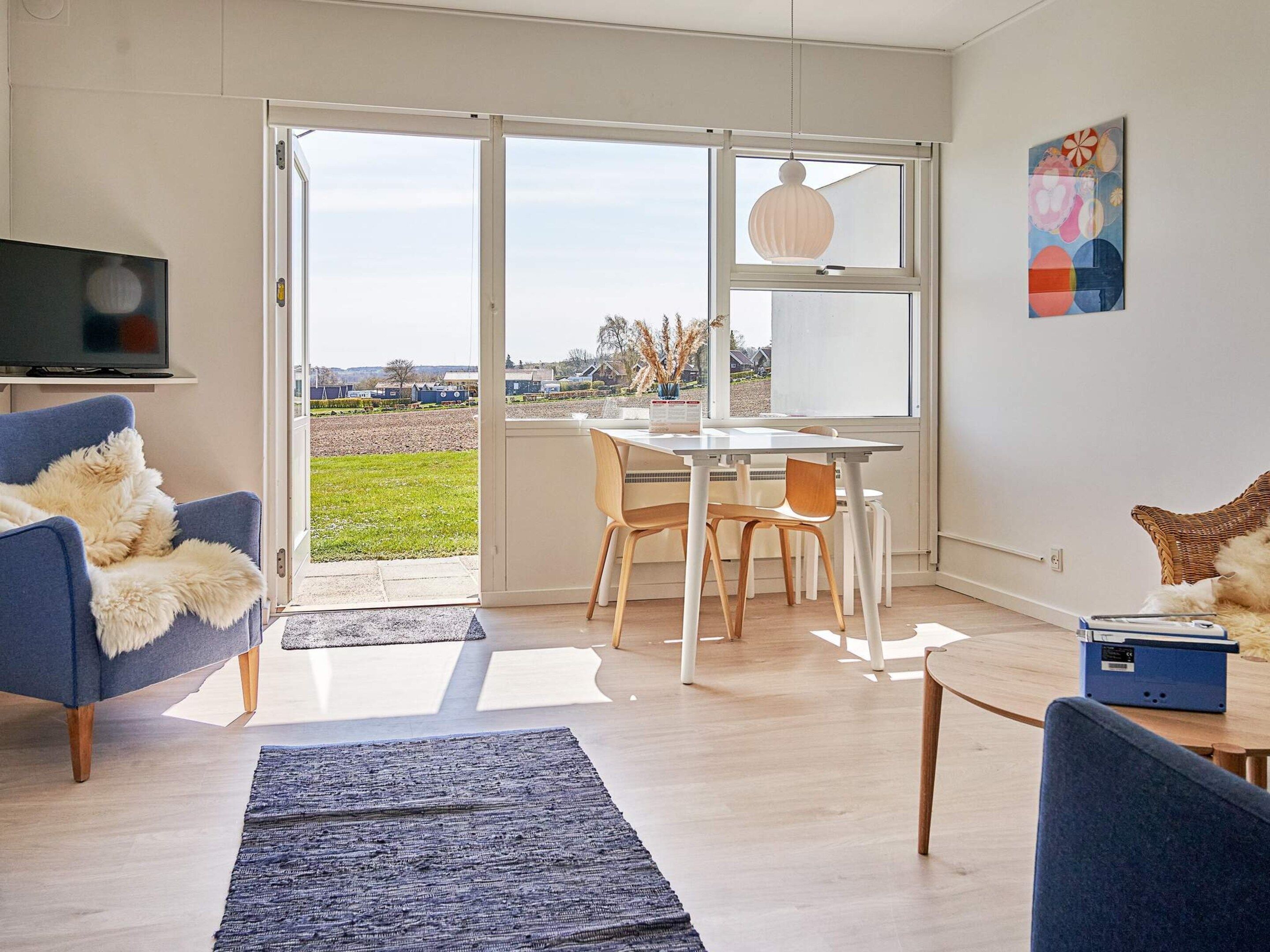 Sala de estar moderna com televisão, sofá, área de jantar com cadeiras e vista através de amplas portas de vidro.