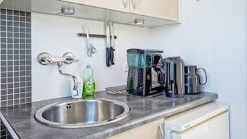 Cozinha com pia de aço inoxidável, cafeteira e chaleira.