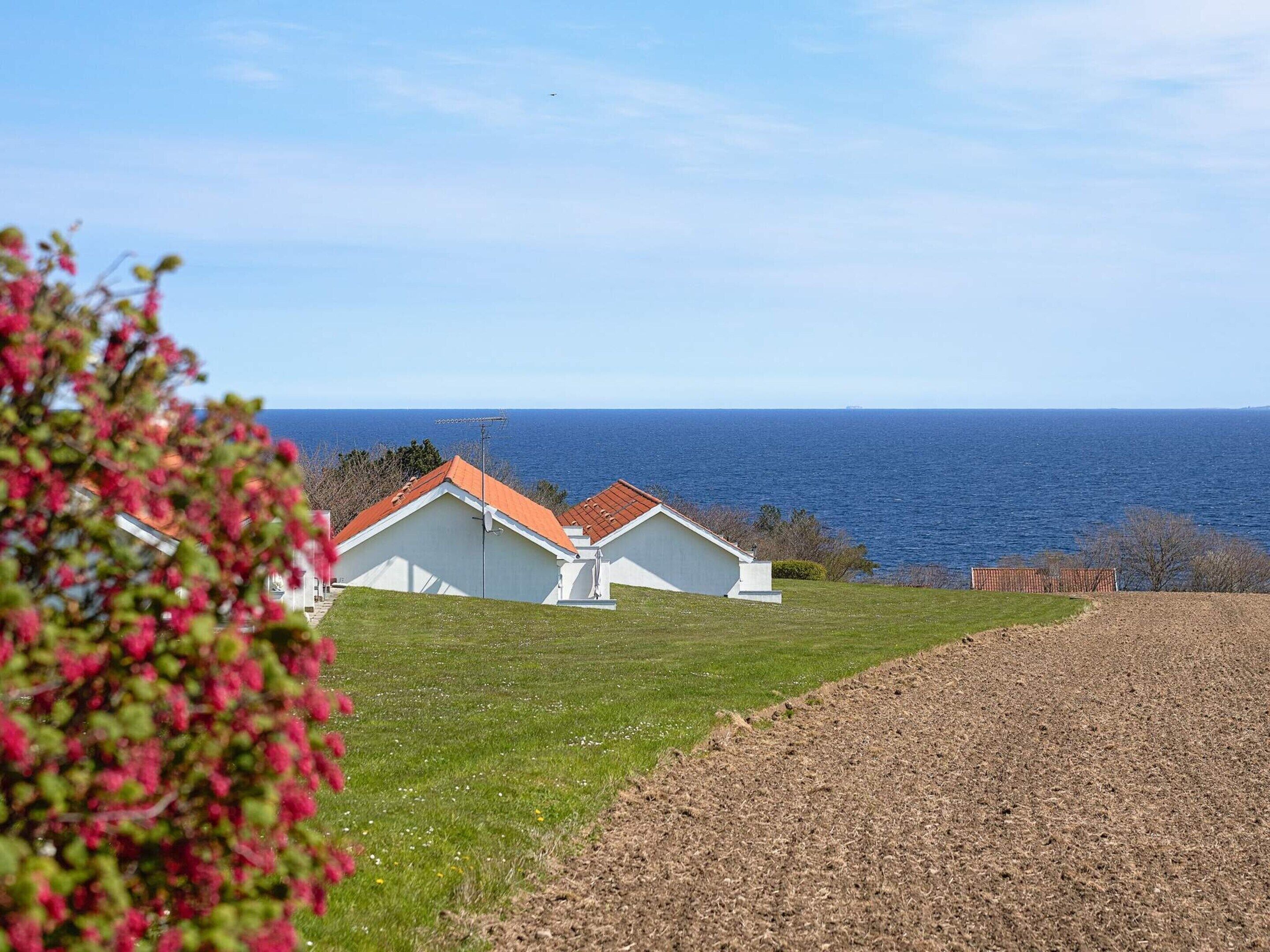 Uma propriedade costeira com edifícios brancos, vista clara para o mar e área gramada.