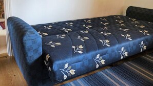 Uma cama com padrão floral, cabeceira azul escura e piso de madeira.