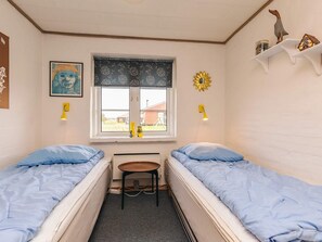 Quarto com duas camas de solteiro, uma mesinha, janela com vista e luminárias na parede.